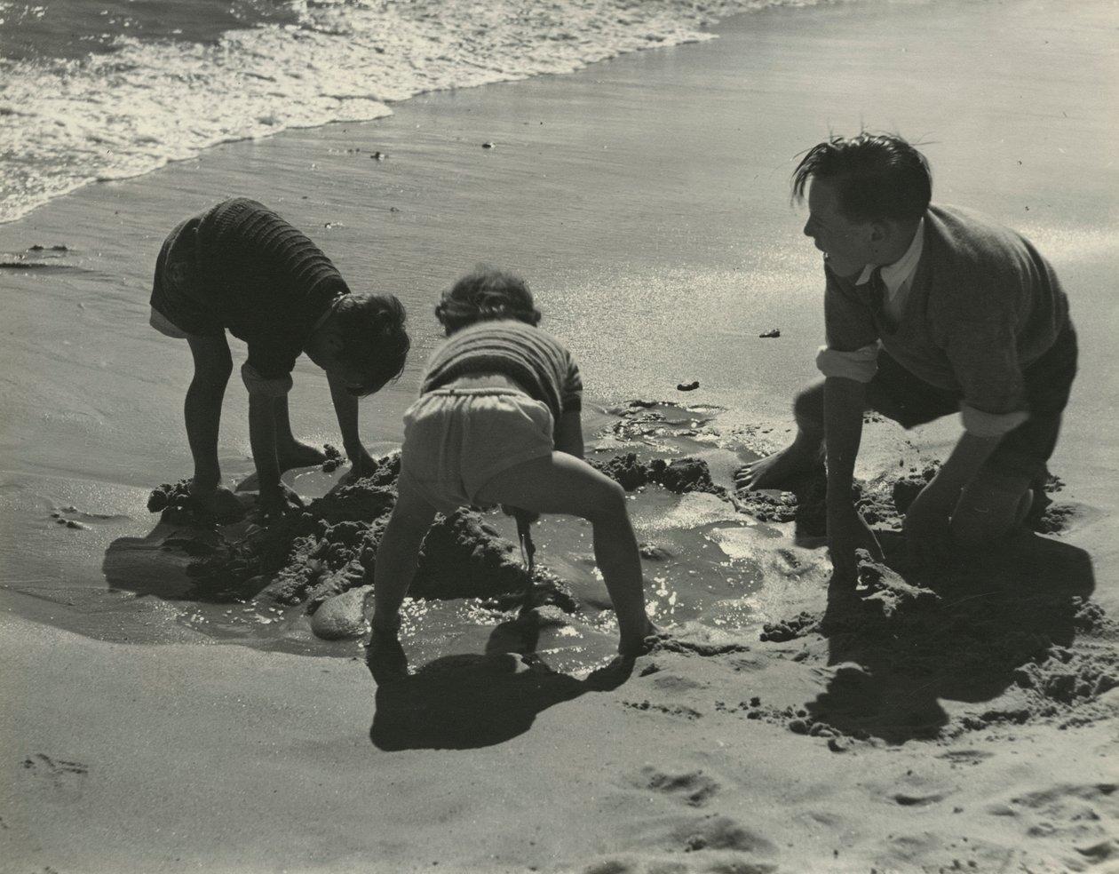 Drei Kinder spielen mit Sand am Strand